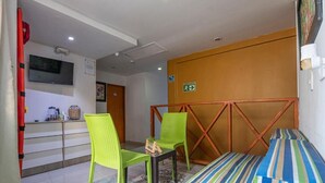 Quarto com cama, duas cadeiras, uma mesinha, televisão e porta com sinalização de saída.