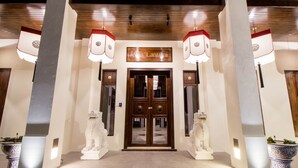 Entrada de hotel com porta de madeira, duas estátuas brancas e uma placa sobre a porta.
