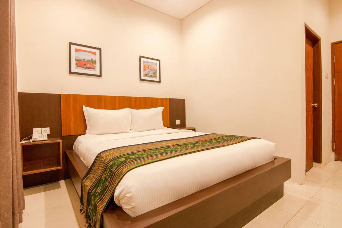 Quarto de hotel com cama, mesa de cabeceira, cabeceira de madeira e duas imagens emolduradas na parede.