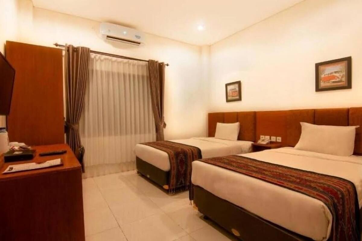 Quarto de hotel com duas camas, uma escrivaninha, ar-condicionado e janela com cortinas.