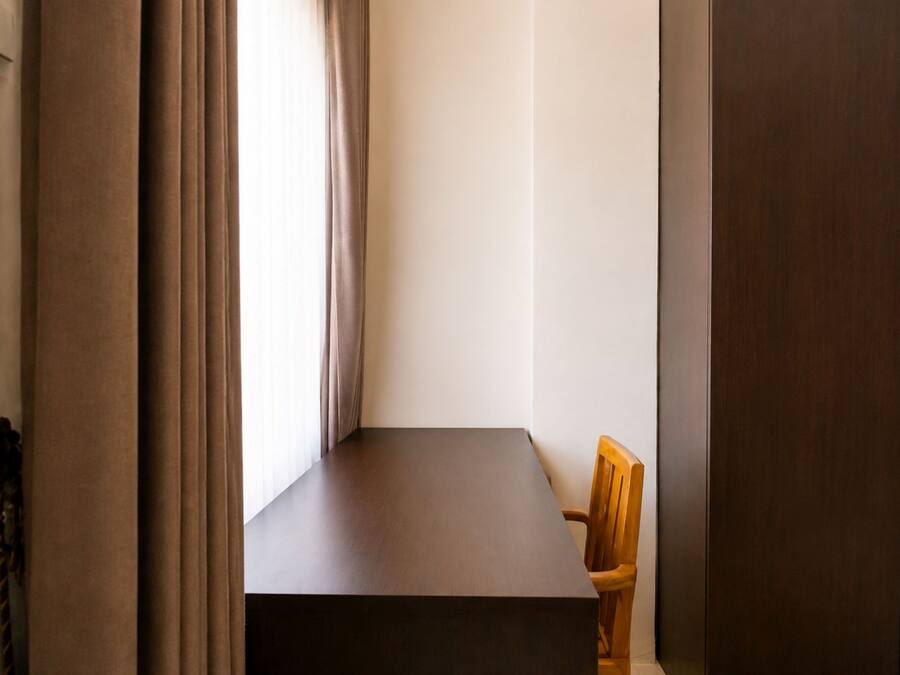 Quarto pequeno com uma cadeira de madeira, uma mesa e uma janela com cortinas.