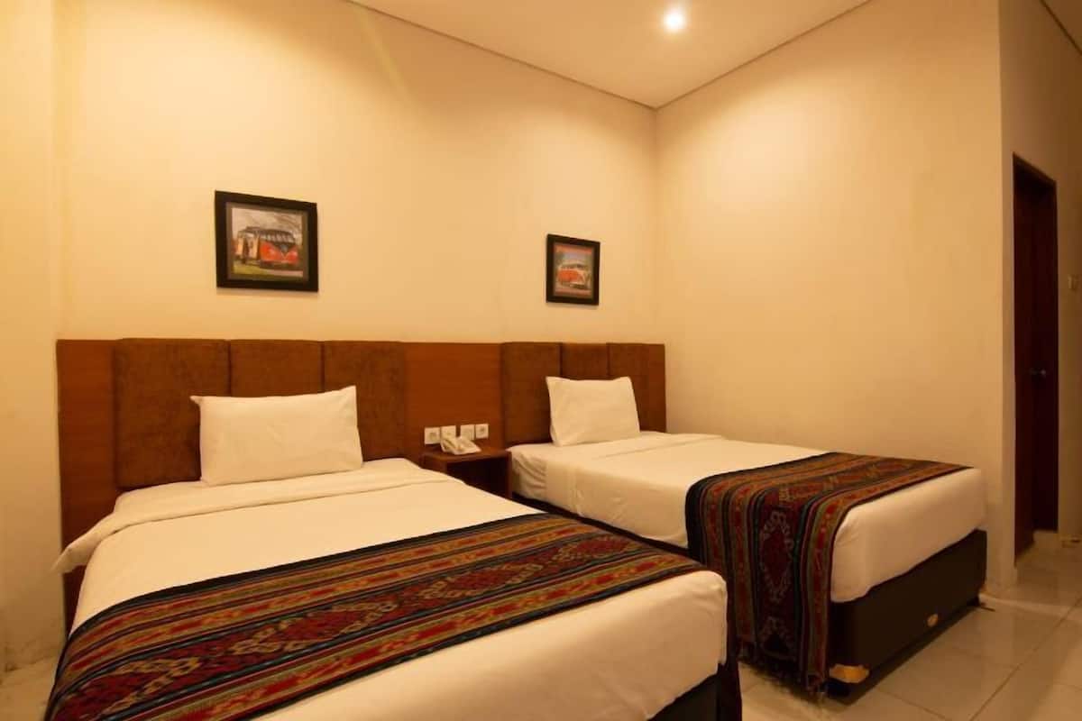 Quarto de hotel com duas camas de solteiro, cabeceira de madeira e uma pequena mesa de cabeceira com telefone.