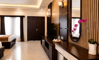 Quarto de hotel com cama, televisão, escrivaninha com espelho e uma orquídea em vaso.