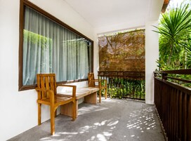 Uma varanda com um banco de madeira, uma janela com cortinas e um cercado de bambu.