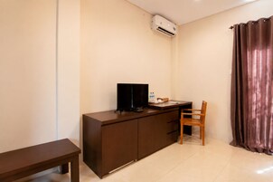 Quarto pequeno e bem organizado com uma escrivaninha de madeira escura, televisão, cadeira e cortina marrom.