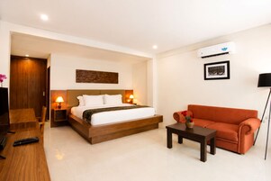 Quarto de hotel com cama, sofá, mesa pequena, televisão e ar condicionado.