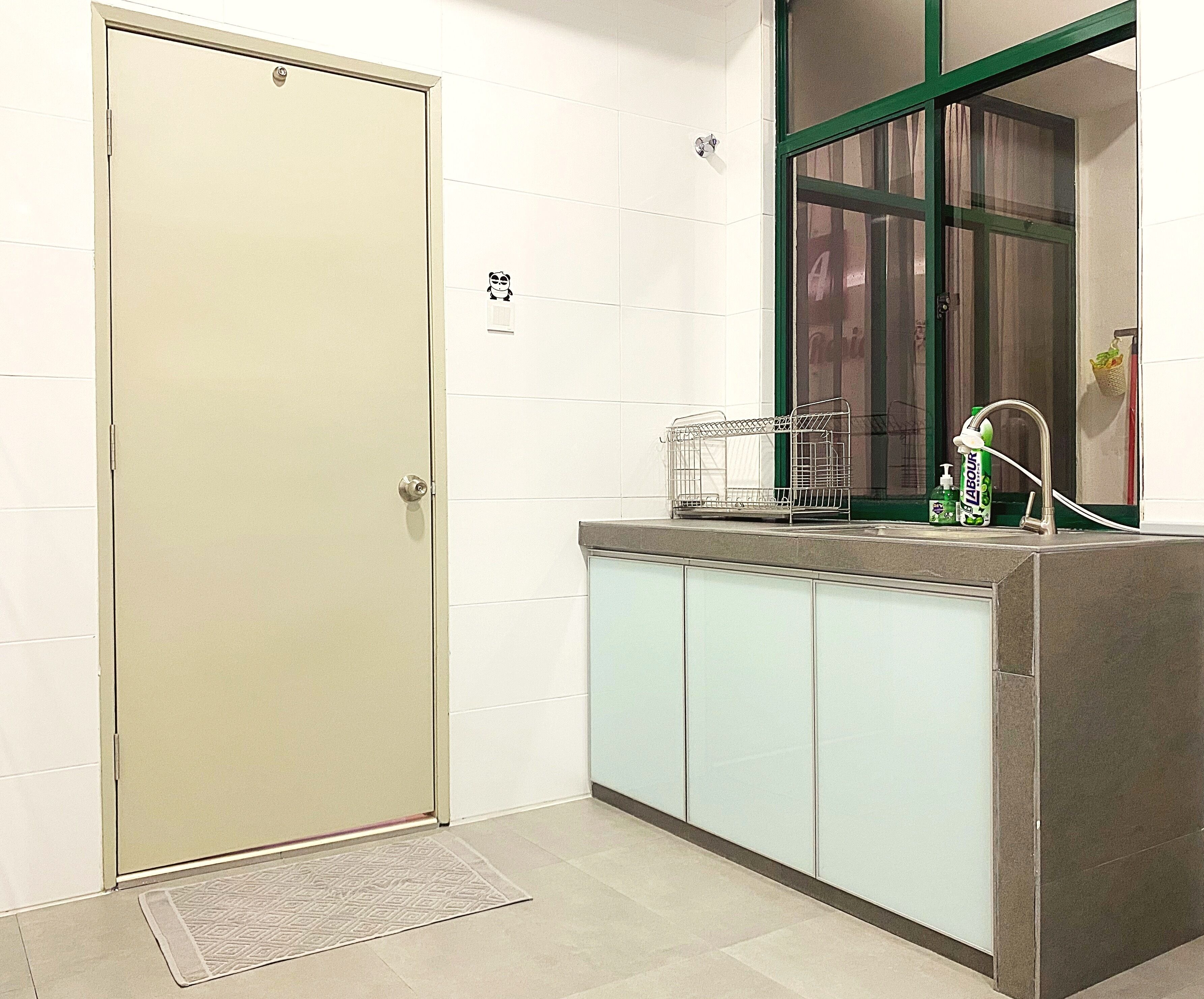 Um banheiro com porta bege, pia com espelho emoldurado em verde e uma pequena janela com vista para o exterior.