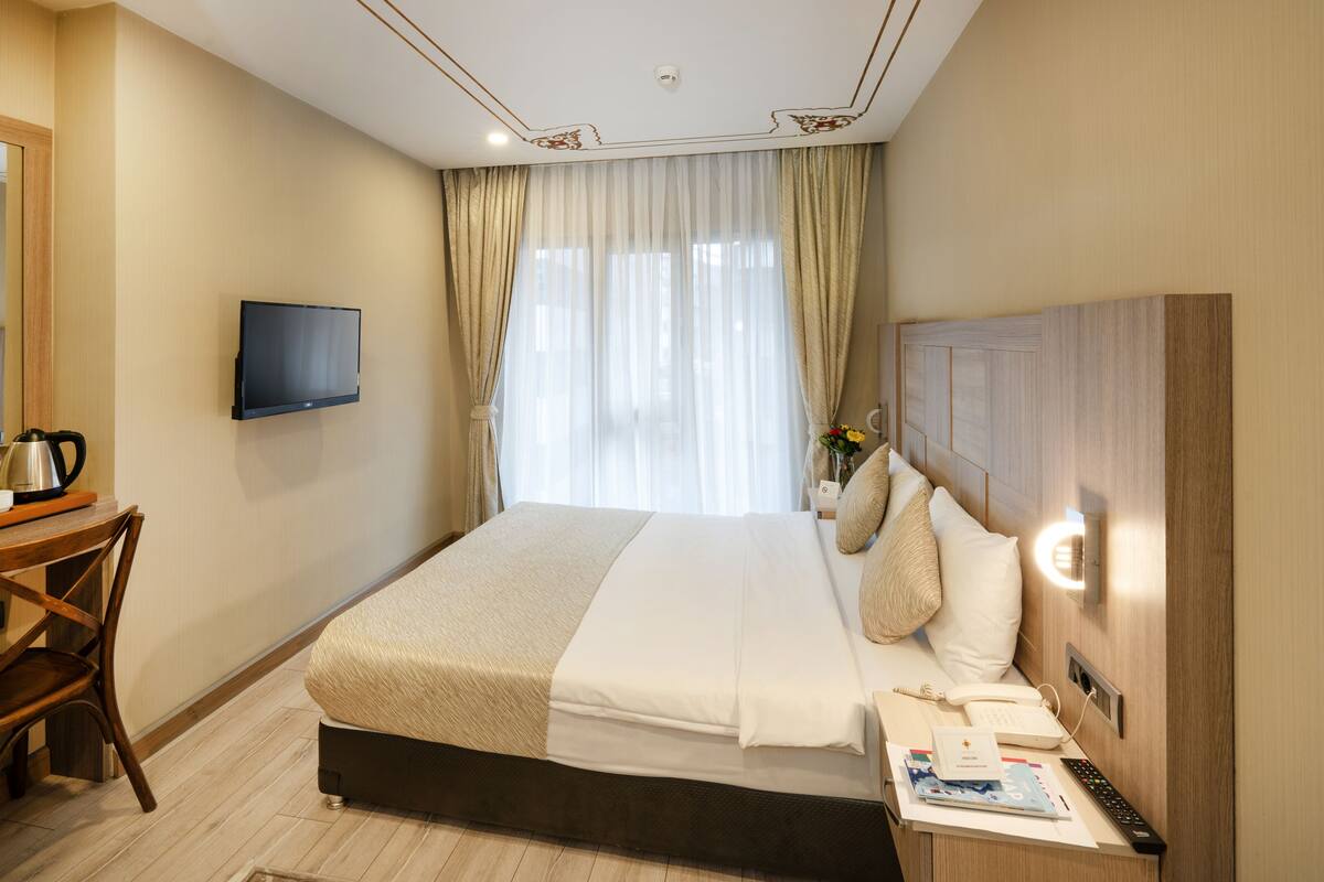 Quarto de hotel com cama, mesa de cabeceira, televisão e escrivaninha com cadeira.