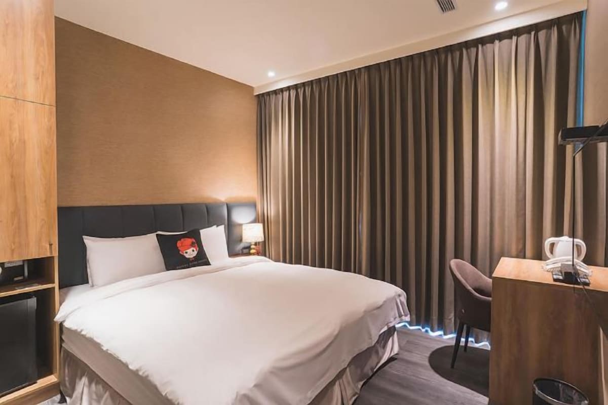 Quarto de hotel com cama, escrivaninha, cadeira e cortina.