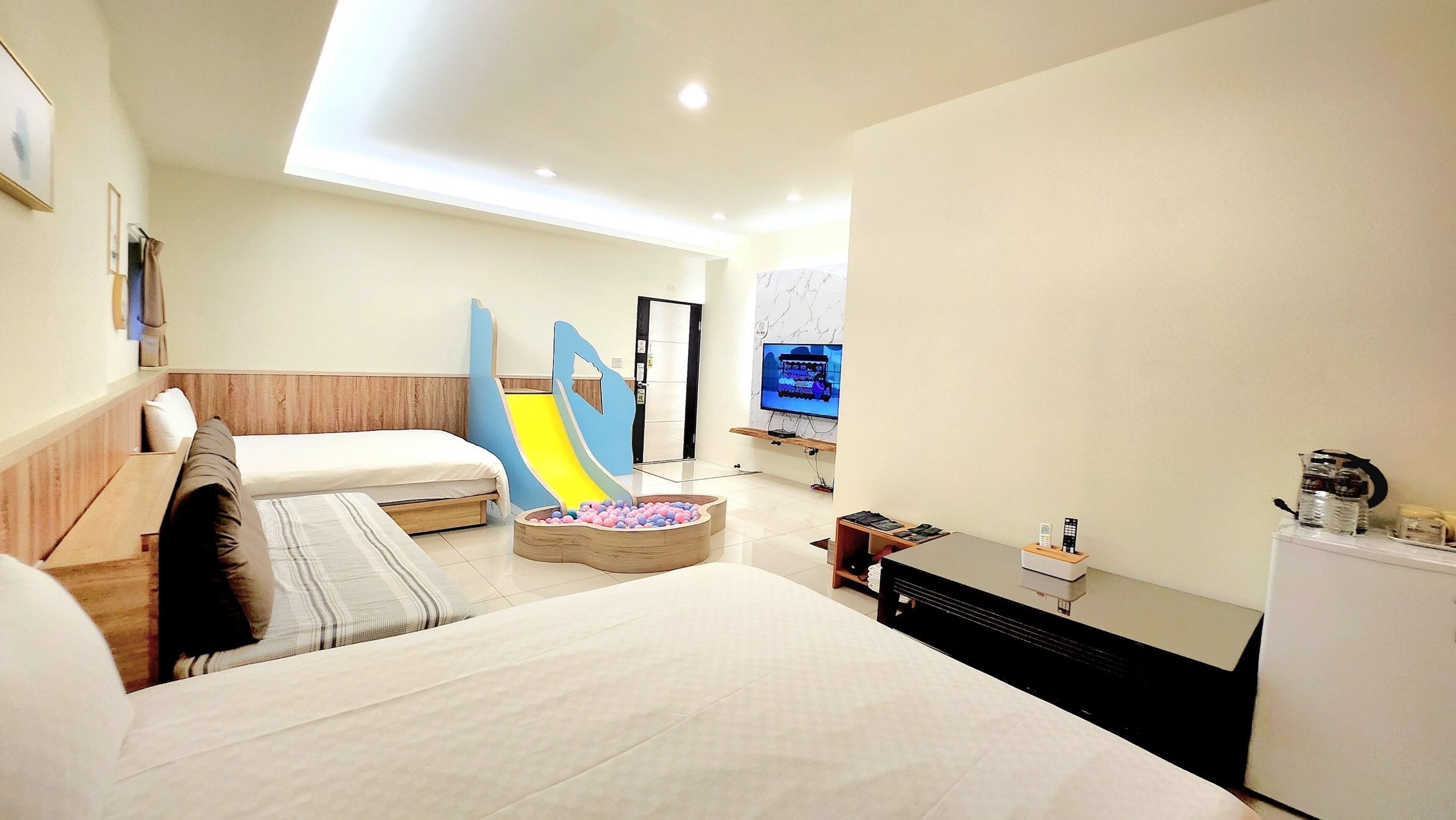 Quarto de hotel com cama, secretária, televisão, um espaço infantil com escorrega e máquina de café.
