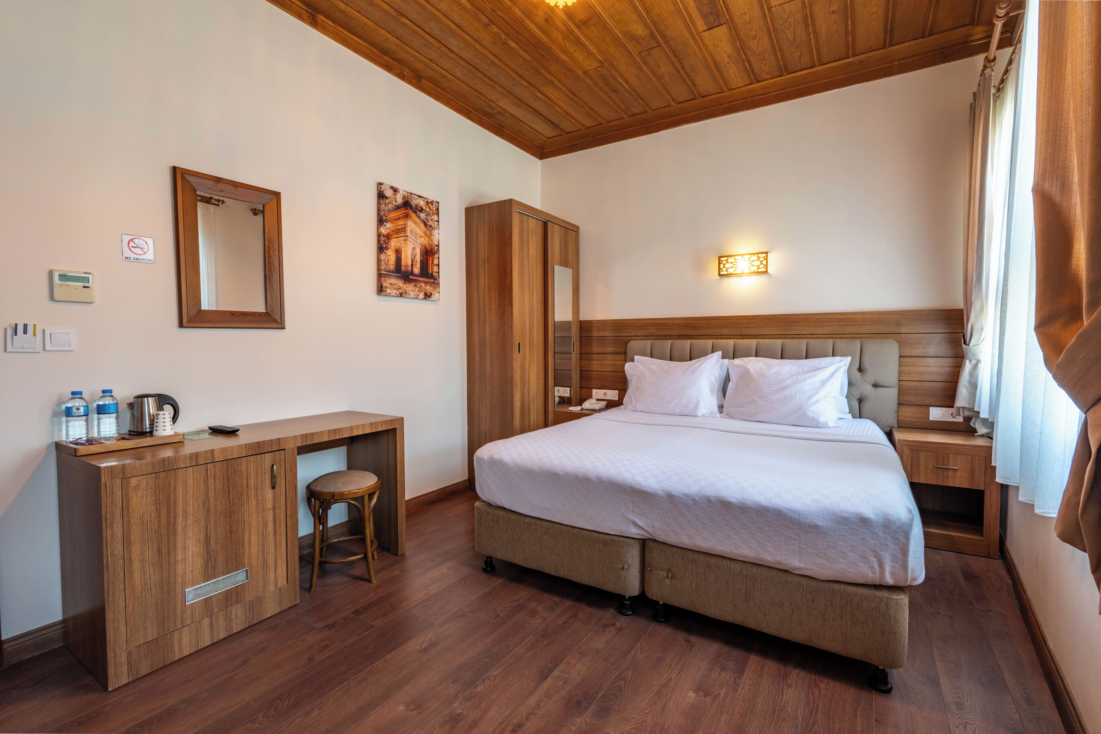 Um quarto com cama, escrivaninha, cadeira, guarda-roupa, espelho e luminária na parede.