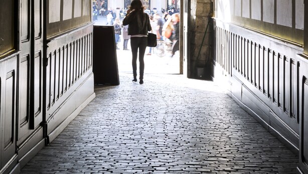 Um corredor com soalho de pedra, teto abobadado e amplas janelas no final.