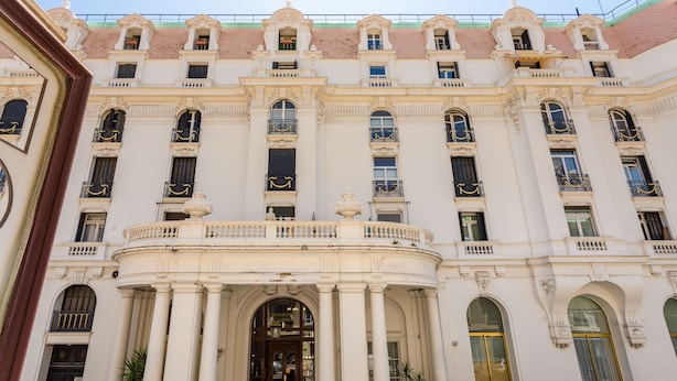 Um edifício imponente com fachada clássica, com diversas janelas e uma entrada central com colunas.