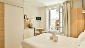 Quarto de hotel com cama, escrivaninha, cadeira, televisão e janela com cortinas.