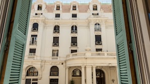Um edifício clássico com várias janelas, uma entrada central e uma varanda com grades.