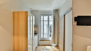 Quarto de hotel com piso de madeira, uma cama, televisão na parede e vista para a varanda.