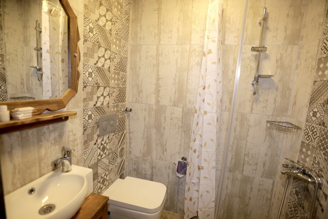 Casa de banho com lavatório, sanita e chuveiro, e azulejos estampados.