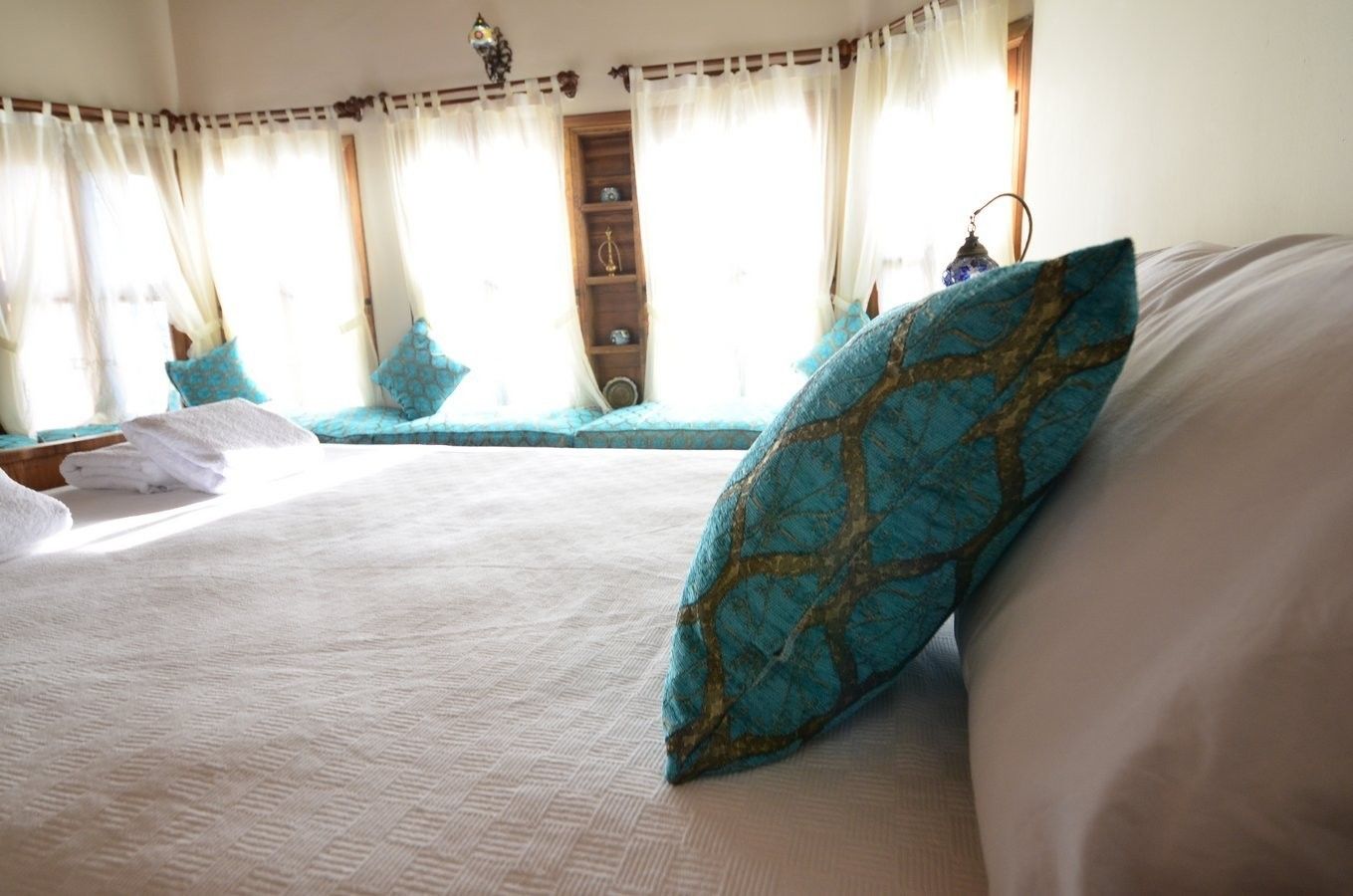 Quarto de hotel com uma cama grande, duas almofadas, uma mesinha de cabeceira e uma janela com cortinas.