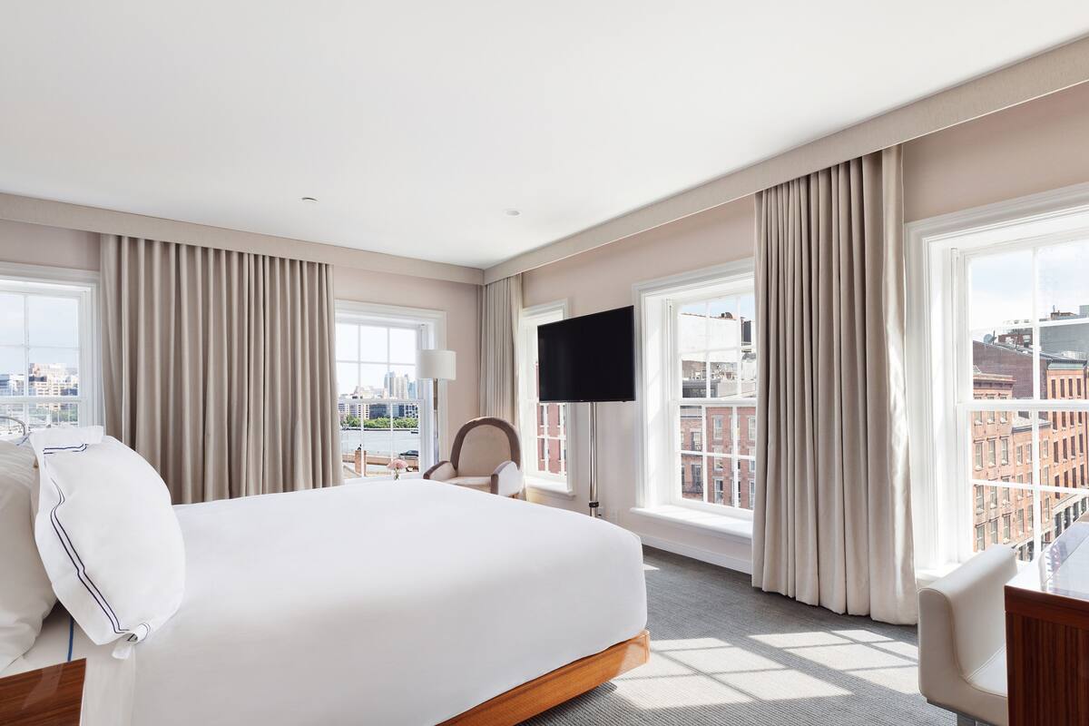 Quarto de hotel com uma cama grande, uma televisão e vista para a cidade.