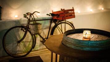 Um interior rústico com uma mesa de madeira, um barril de metal, uma bicicleta e uma caixa vermelha.