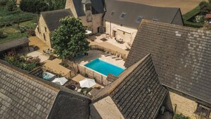 Uma casa grande com piscina, cercada por um quintal murado e um campo.