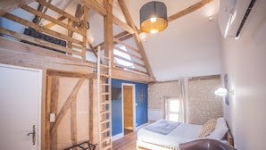 Um quarto com um mezanino, vigas de madeira, uma escada, uma cama, uma cadeira e um lustre.