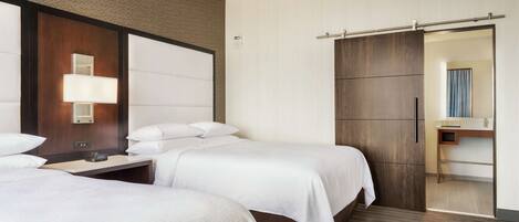 Quarto de hotel com duas camas, uma mesa de cabeceira com abajur, um espelho grande e um guarda-roupa com porta deslizante.