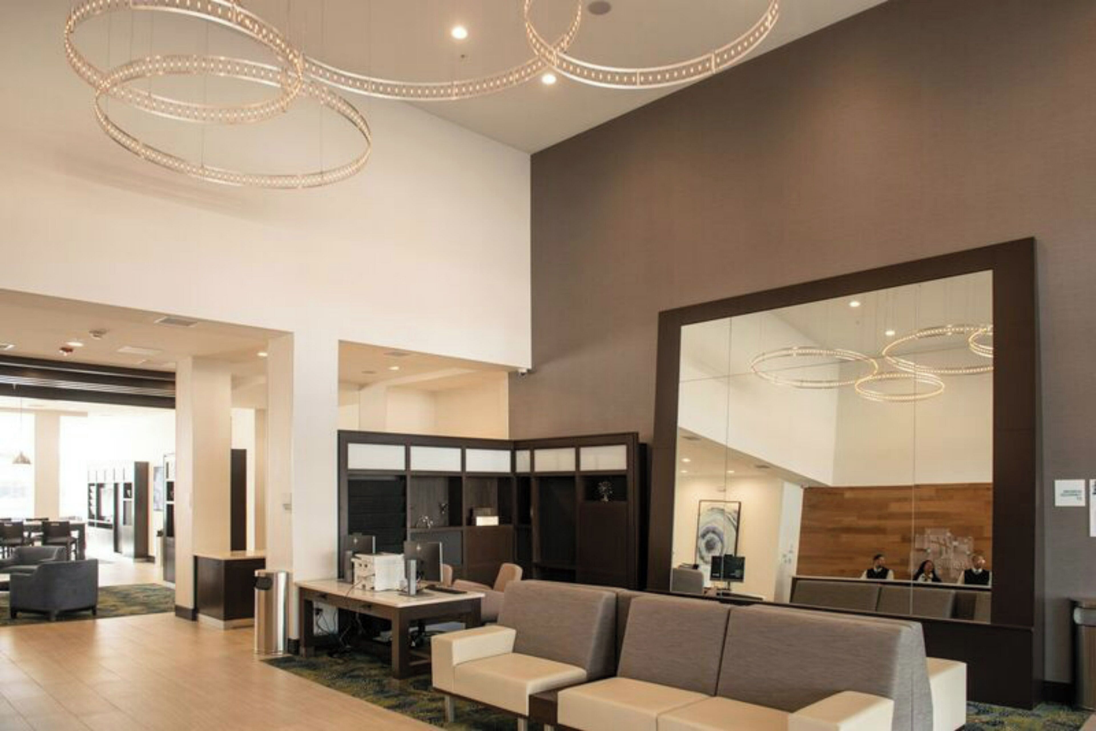 Um lobby moderno com área de estar, um espelho grande refletindo o design do teto e um balcão de recepção.