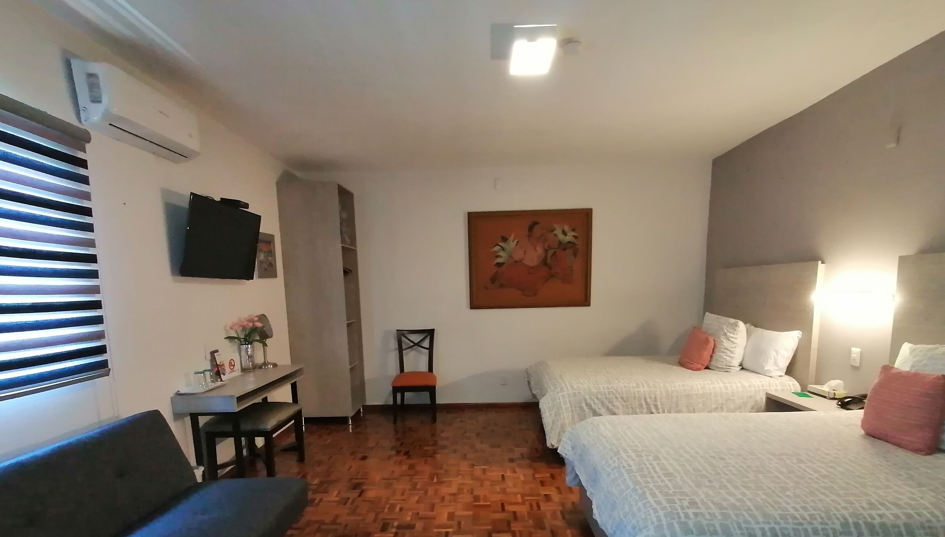 Quarto de hotel com duas camas, uma escrivaninha, uma cadeira, uma televisão e um quadro na parede.