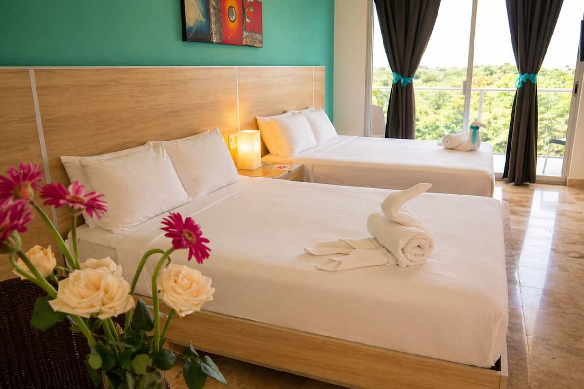 Quarto de hotel com duas camas, cabeceira de madeira, um quadro na parede e vista para o verde lá fora.