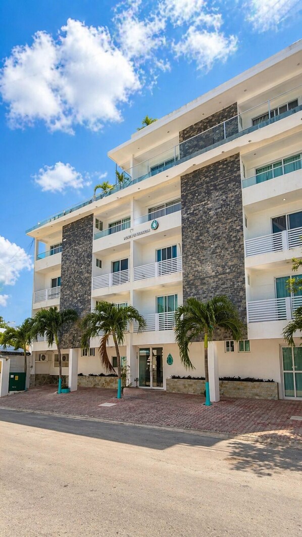Um hotel com vários andares, fachada de pedra, varandas e palmeiras.