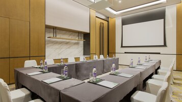 Uma sala de conferências com uma mesa comprida, cadeiras, garrafas de água e uma tela de projetor.