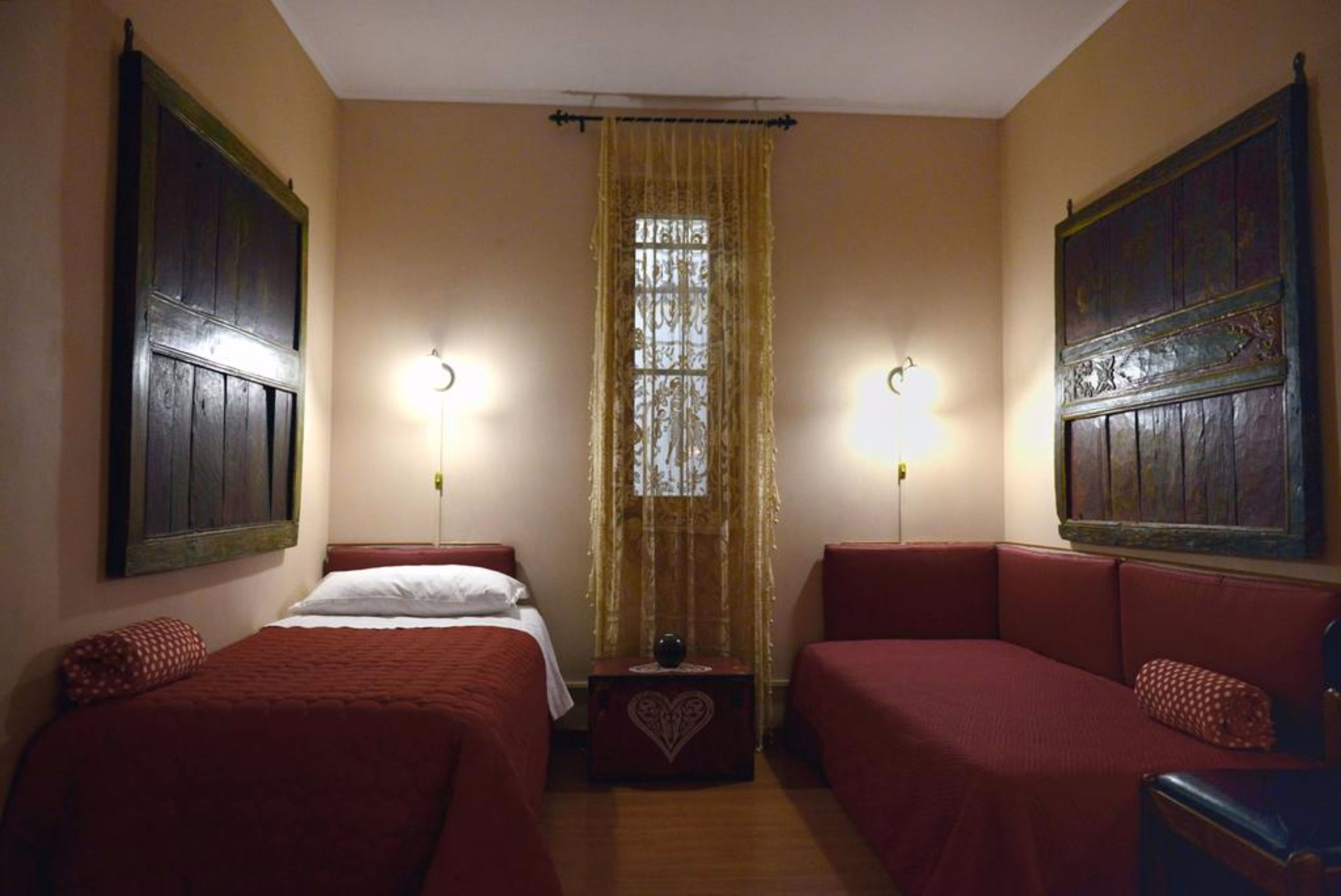 Quarto com duas camas, janela com cortinas e luminárias fixadas na parede.