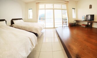Quarto de hotel com duas camas, piso de madeira, televisão e vista para o exterior através de uma grande janela.