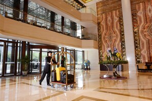 Um hall espaçoso com teto alto, uma escadaria imponente e um grande balcão de recepção.