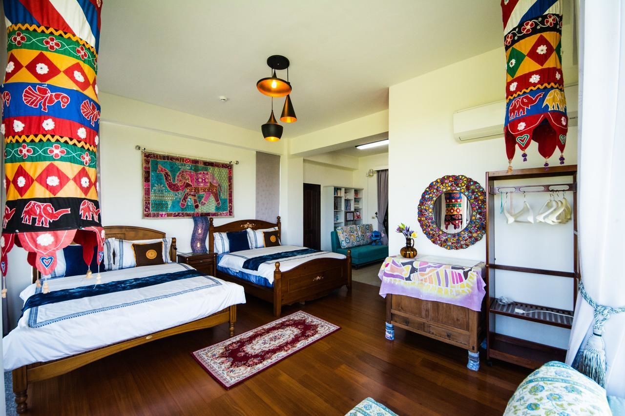 Quarto com duas camas de madeira, uma cômoda de madeira, uma tapeçaria colorida e um candeeiro suspenso.