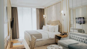 Quarto de hotel com uma cama grande, área de estar, espelho e televisão.