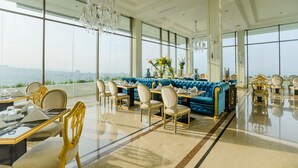Uma sala de jantar ampla com um sofá azul, cadeiras douradas e lustres.