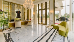 Um hall amplo com piso de mármore, um lustre, balcão de recepção e janelas grandes com vista para o exterior.