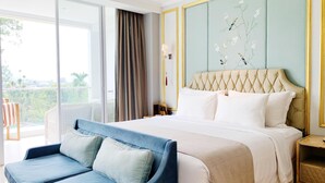 Quarto de hotel com uma cama grande, um sofá azul, uma varanda com vista e uma parede com papel de parede floral.