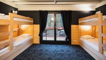Quarto com duas beliches, janela com cortinas e vista para um estacionamento, além de piso coberto por carpete.