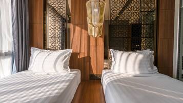 Quarto de hotel com duas camas, painéis de madeira, luminária pendente e divisória com padrão.