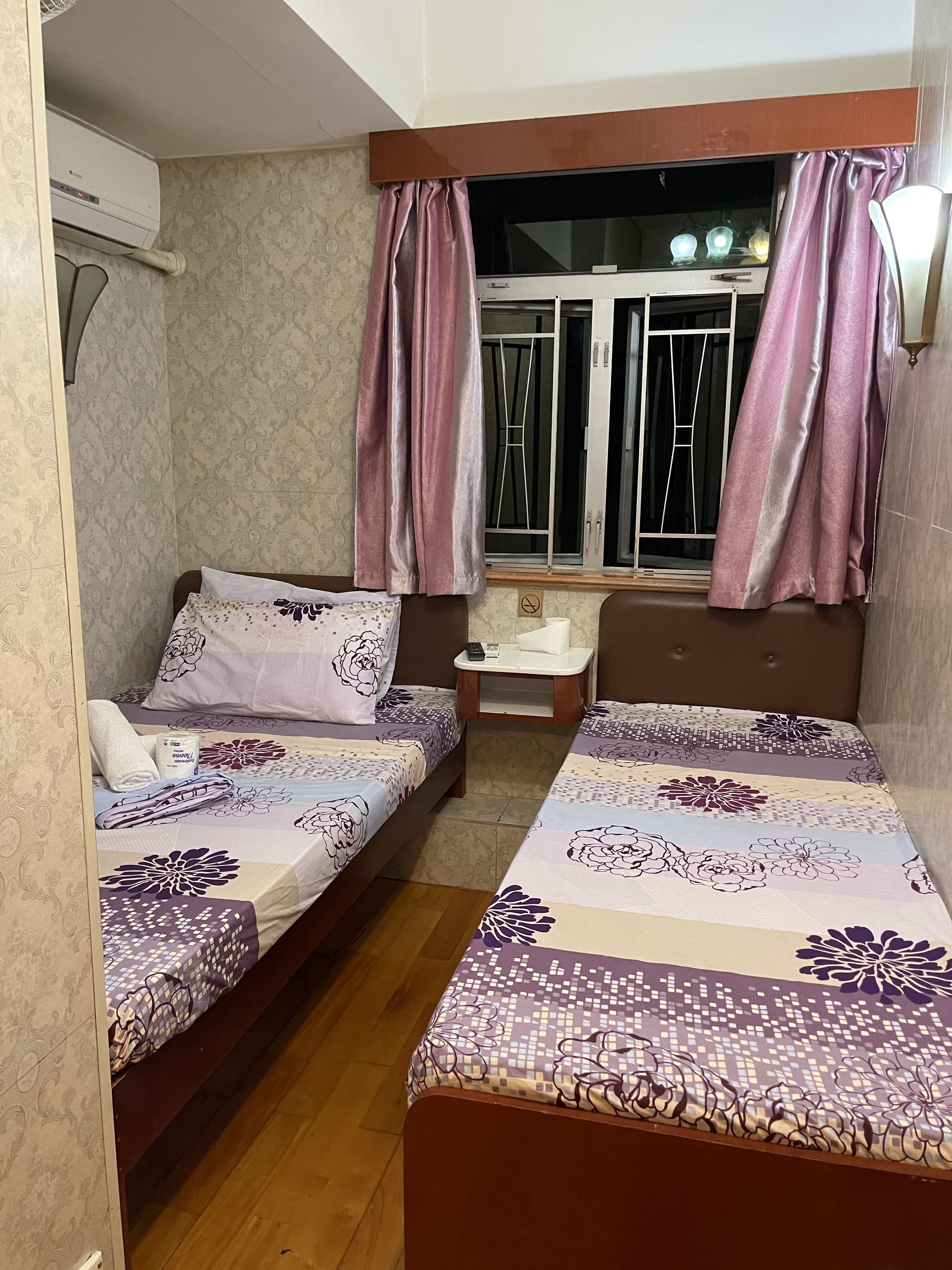 Quarto com duas camas de solteiro, uma mesinha e uma janela com cortinas.