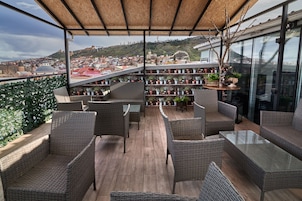 Varanda com móveis de vime, plantas em vasos e vista para a paisagem urbana.