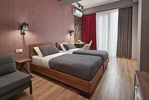 Quarto de hotel moderno com cama de madeira, escrivaninha, cadeira e estante.
