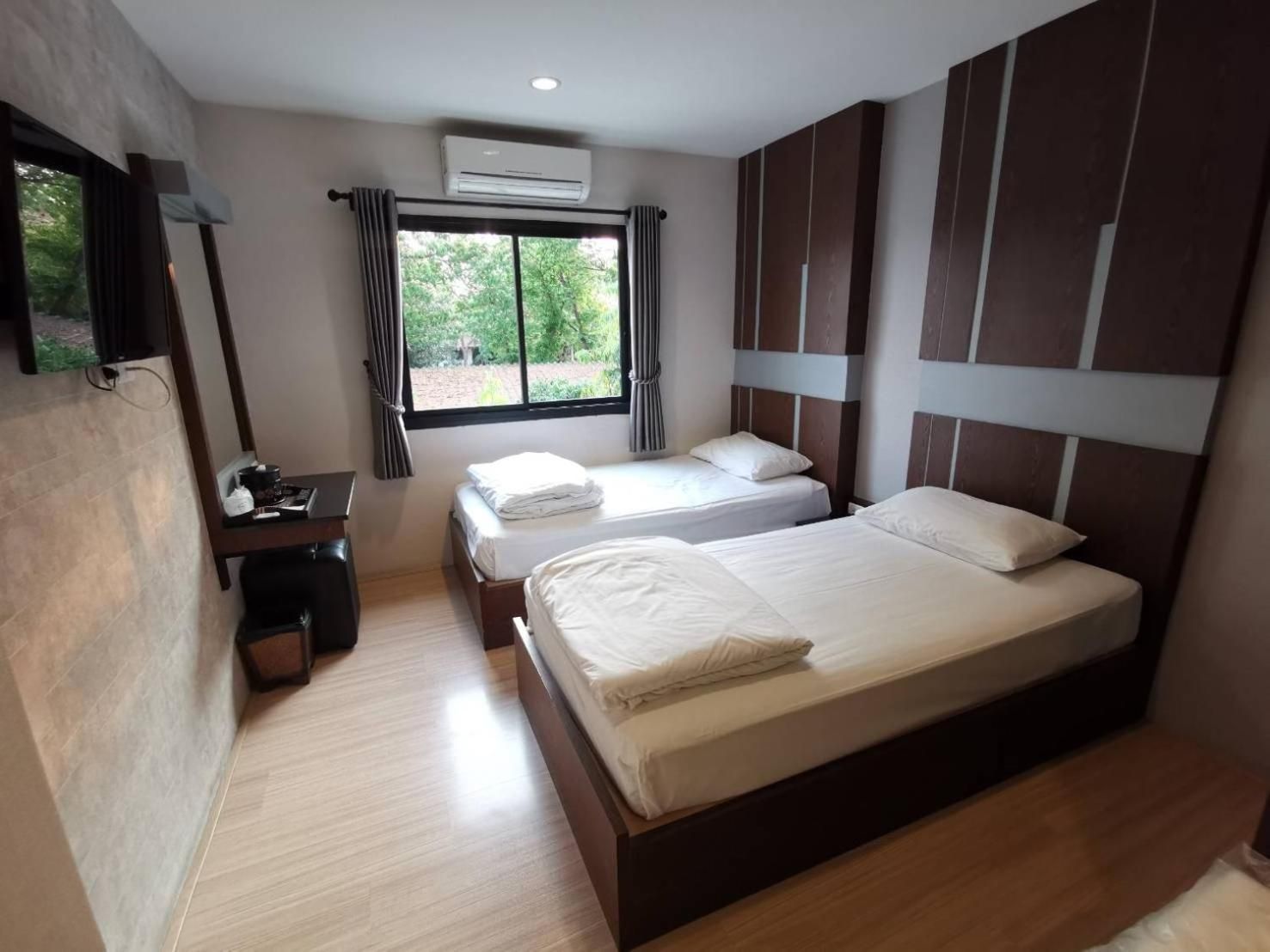 Quarto de hotel com duas camas, televisão de tela plana, aparelho de ar condicionado e janela com cortinas.