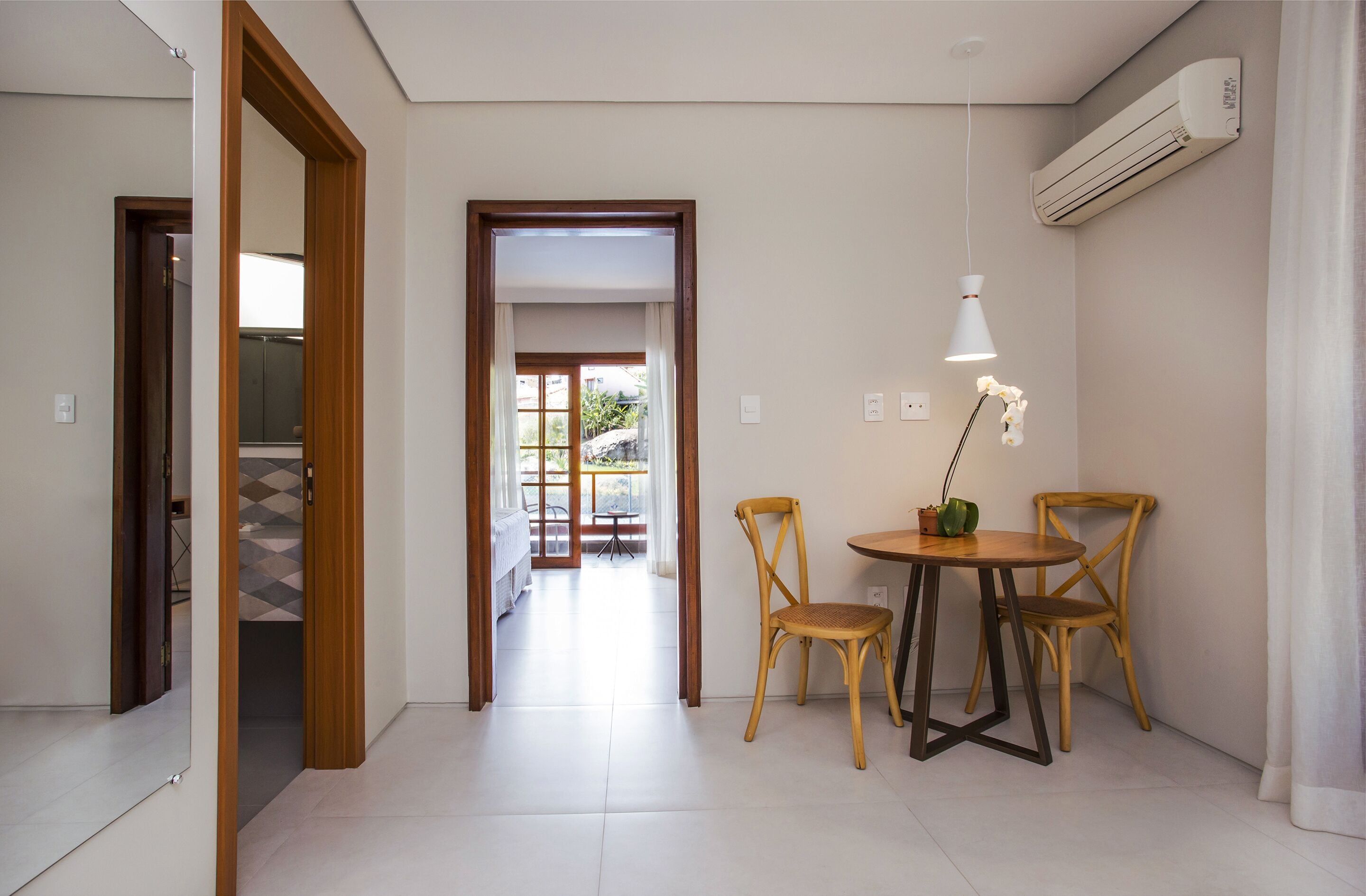 Um interior moderno com área de jantar, apresentando uma mesa redonda e duas cadeiras, uma luminária pendente e um aparelho de ar condicionado na parede.
