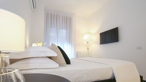 Quarto de hotel com cama, mesa de cabeceira, luminária e televisão fixada na parede.