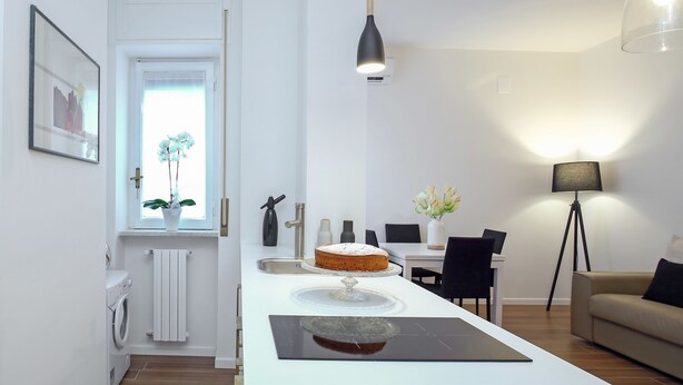 Cozinha moderna com ilha central, área de jantar com mesa e cadeiras, e um sofá na sala de estar.