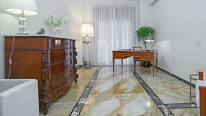 Quarto com cómoda de madeira, escrivaninha, luminária, planta em vaso e chão de mármore.
